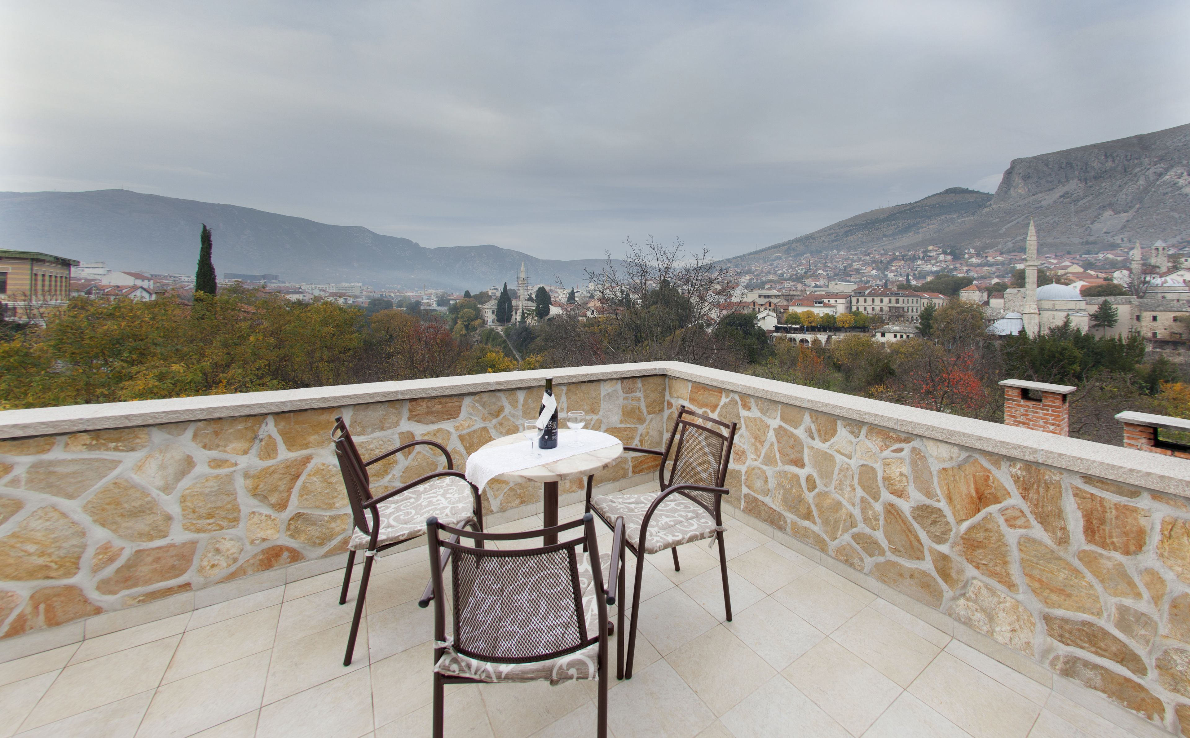 Terraço de lajes de pedra com uma mesa e cadeiras, com vista para um horizonte urbano e montanhas ao fundo.