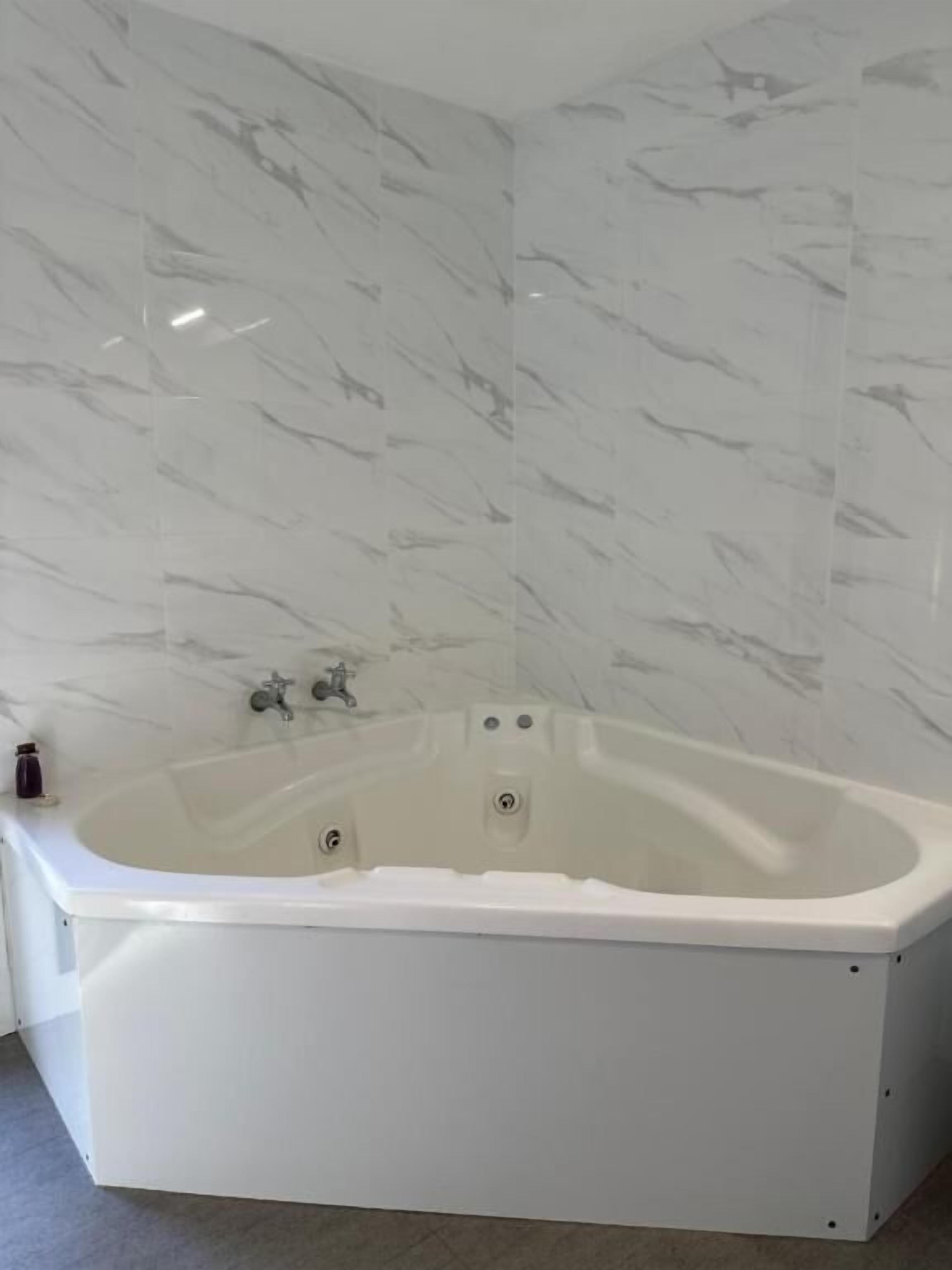 Um banheiro moderno com uma banheira independente, paredes de mármore e uma pequena garrafa de shampoo ao lado.