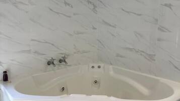 Um banheiro moderno com uma banheira independente, paredes de mármore e uma pequena garrafa de shampoo ao lado.
