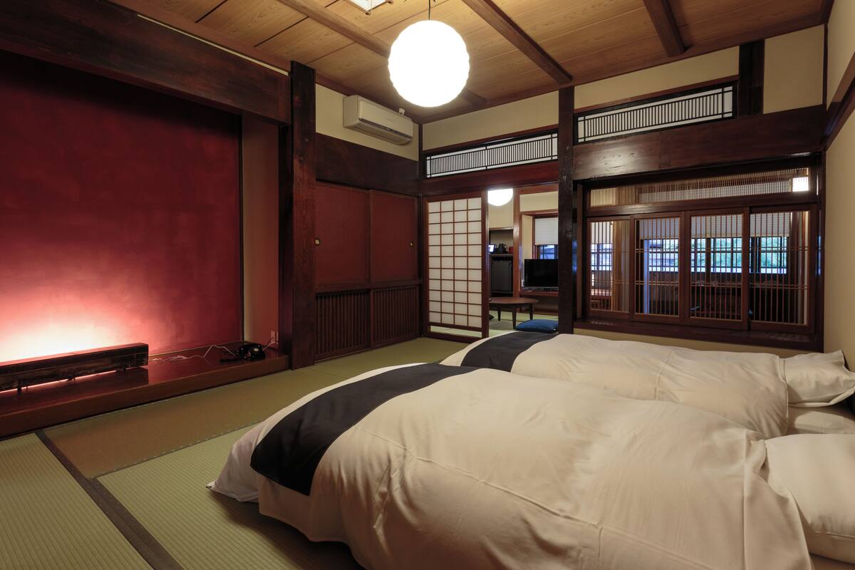 Um quarto japonês tradicional, com tatames, cama baixa de madeira, portas deslizantes e vista através de um shoji.