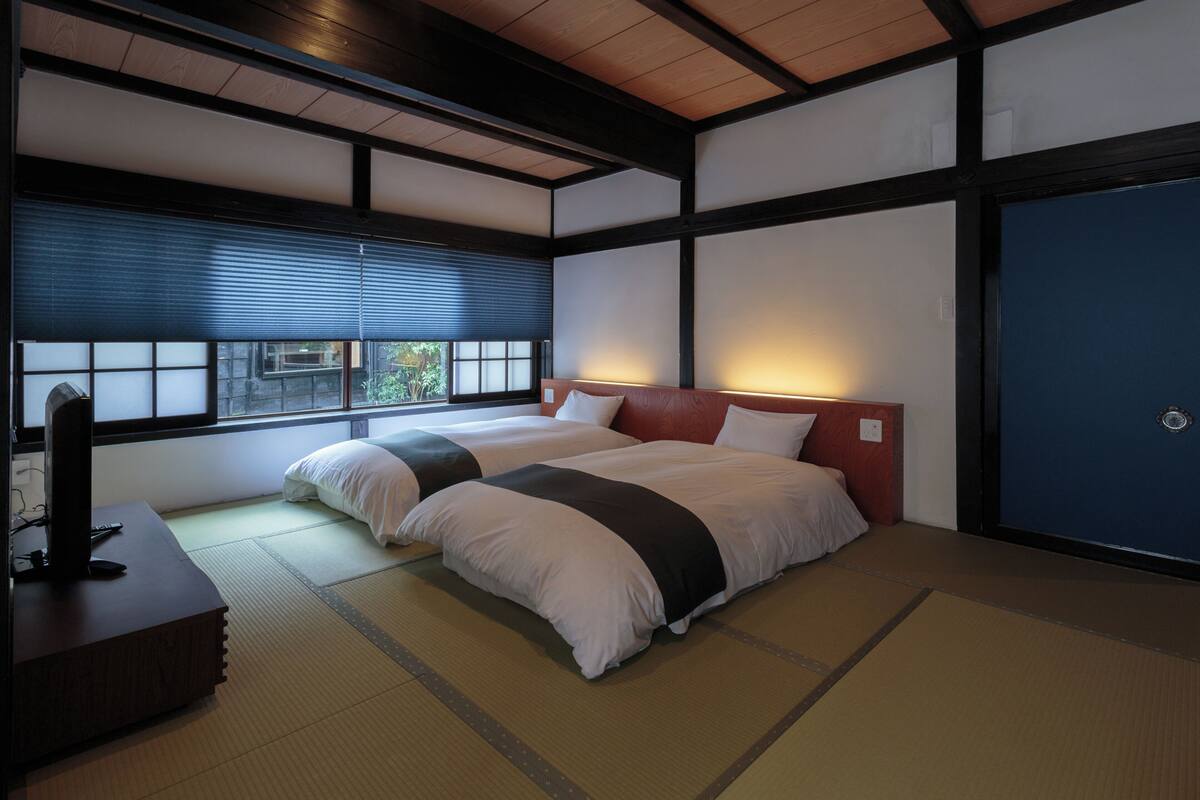 Quarto japonês tradicional com tatames, futon, televisão sobre uma mesa baixa e porta de correr.