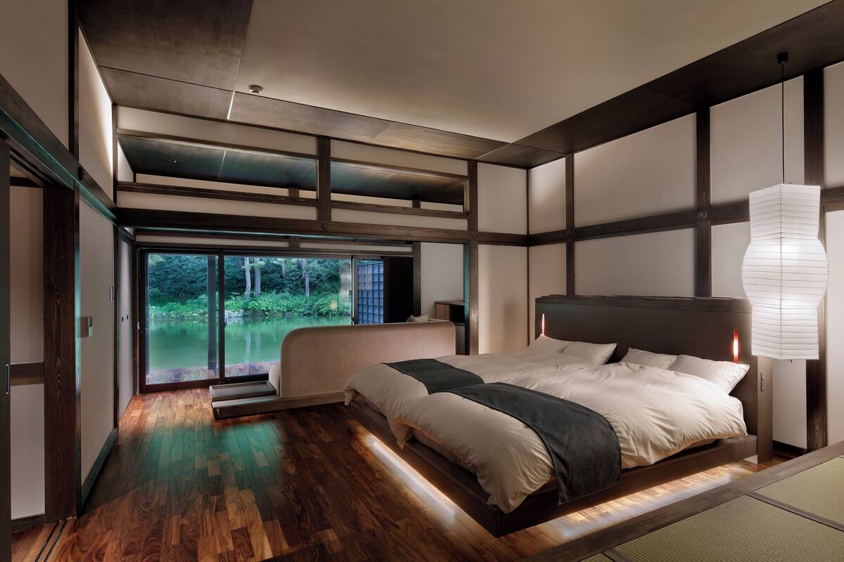 Quarto com cama, janela e vista para área verde.