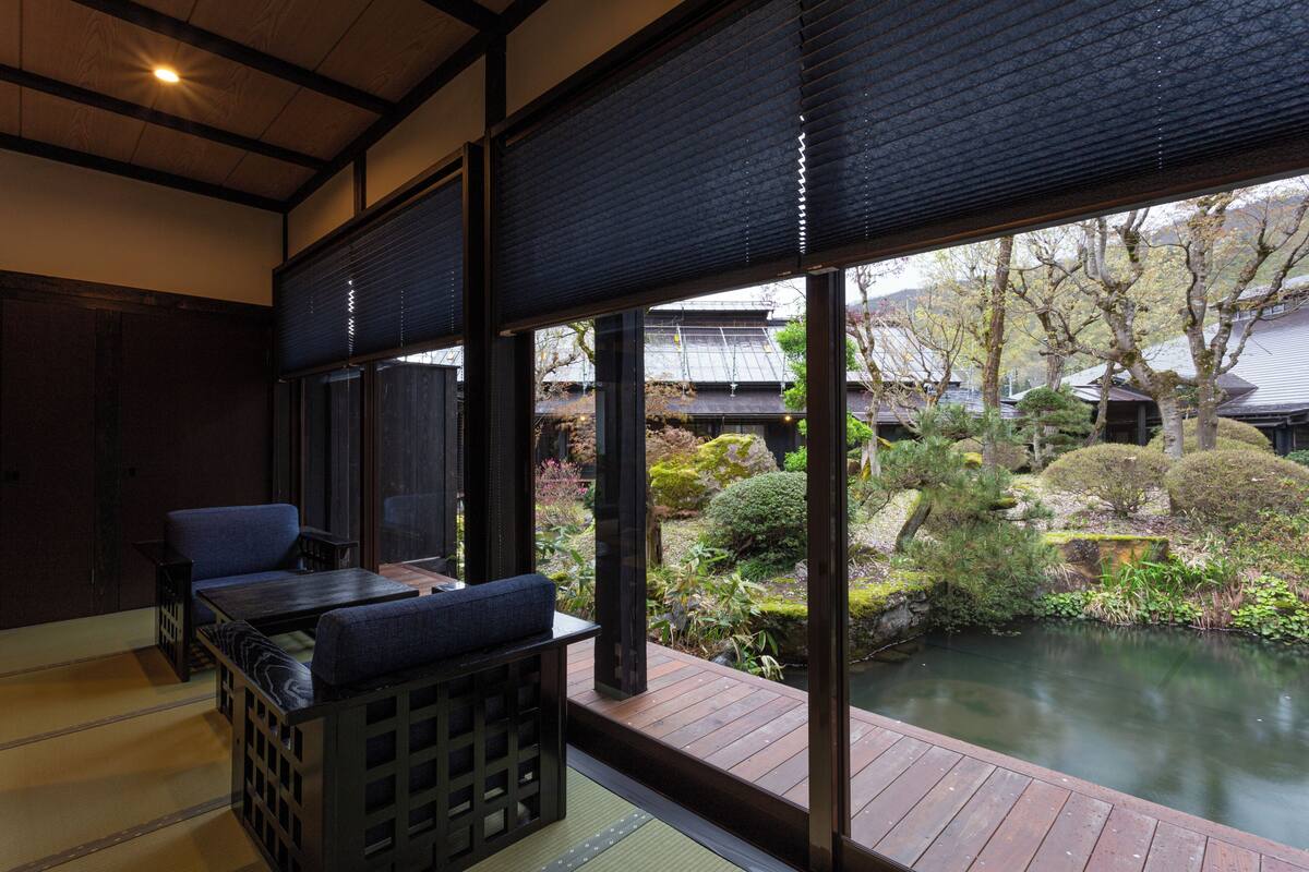 Um quarto japonês tradicional com tatames, uma mesa de madeira baixa e vista para um jardim com lago.