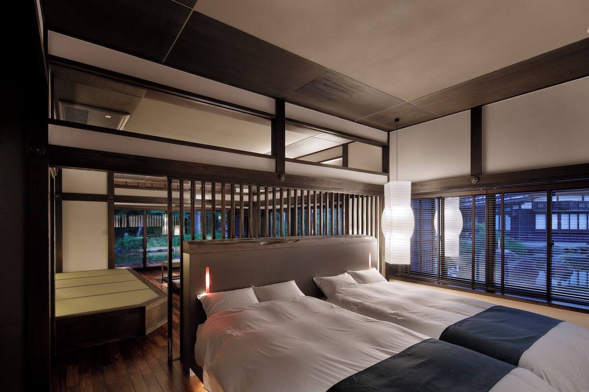Quarto de hotel moderno com uma cama grande, uma escrivaninha e vista para a cidade através de amplas janelas.