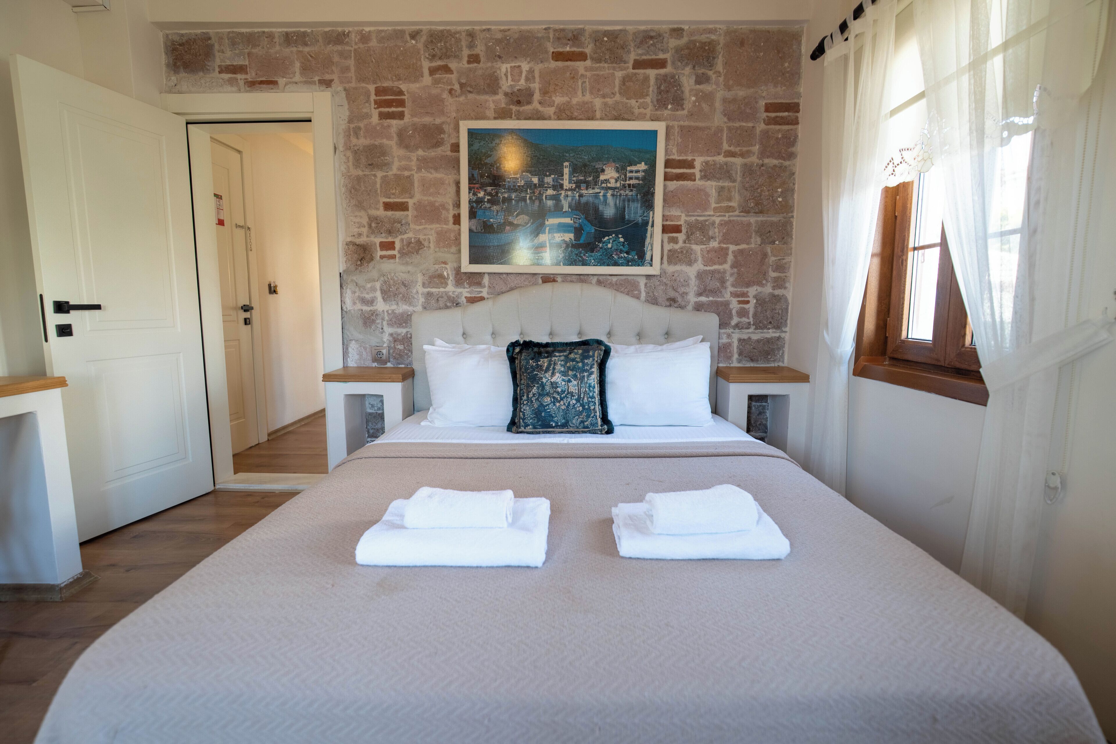 Quarto de hotel com uma cama grande, parede de pedra, um quadro e uma janela com cortinas.