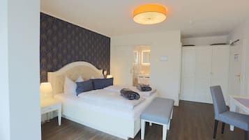 Quarto de hotel com uma cama grande, uma mesa de cabeceira com abajur, um banco, uma cadeira e um guarda-roupa.