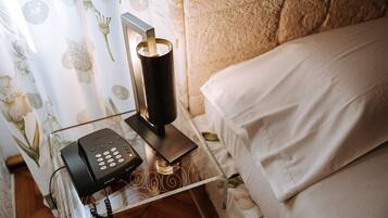 Uma mesa de cabeceira com uma luminária, um controle remoto e um recipiente de vidro.