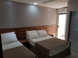 Quarto de hotel com duas camas de solteiro, cabeceiras de madeira e uma janela grande.