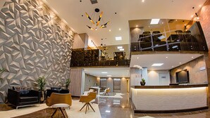 Um lobby moderno com design geométrico na parede, um balcão de recepção e uma área de estar com cadeiras.