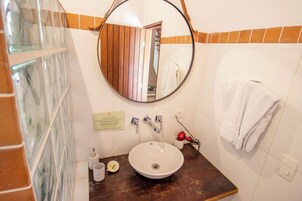 Casa de banho com espelho redondo, lavatório branco, porta-toalhas e cabine de duche em vidro.