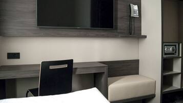 Quarto de hotel moderno com uma cama, uma mesa de escritório, uma cadeira, uma TV fixada na parede, um telefone e uma pequena prateleira com micro-ondas.