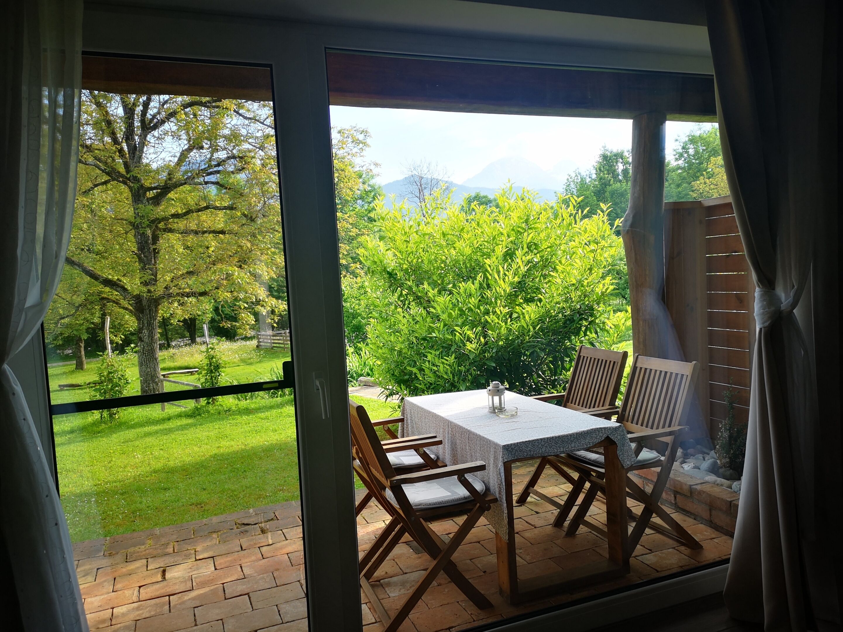 Uma varanda com mesa e cadeiras, vista para um jardim verde e uma montanha ao longe.