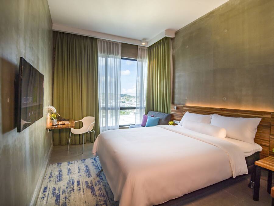 Quarto de hotel com uma cama grande, uma escrivaninha com cadeira, uma televisão e vista para a cidade.