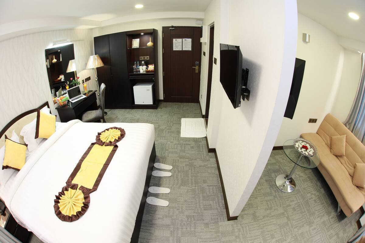 Quarto de hotel com cama, escrivaninha, cadeira e sofá.
