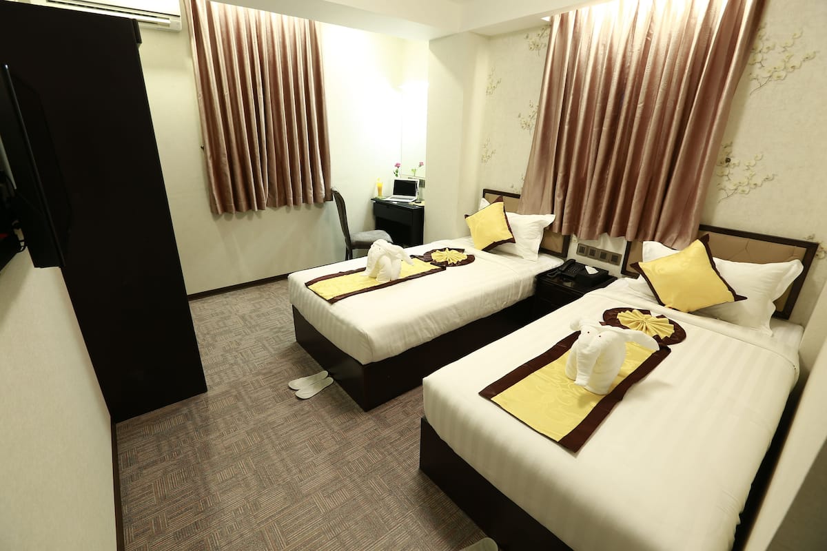 Quarto de hotel com duas camas, cada uma com uma toalha e um objeto decorativo. Há uma mesa com um laptop e uma cadeira.