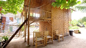 Estrutura de bambu com telhado de palha, duas cadeiras de vime e uma escada.