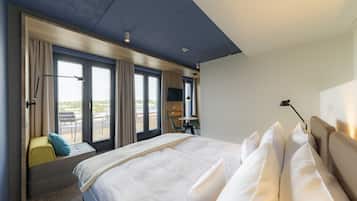 Quarto de hotel moderno com uma cama grande, uma escrivaninha e vista para o exterior por grandes janelas.
