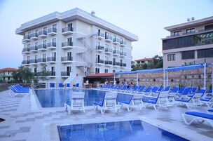 Uma piscina com espreguiçadeiras azuis, um edifício com varandas e uma parede de pedra.