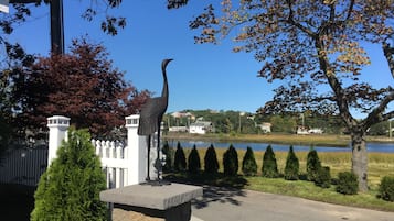 Um parque com uma estátua de um pássaro sobre um pedestal, um lago e casas ao fundo.