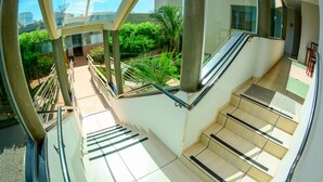Interior moderno com escadaria de vidro que dá para área externa com vegetação e céu claro.