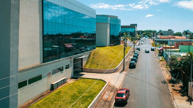 Um edifício moderno com grandes janelas de vidro, estrutura curva e estacionamento com carros.