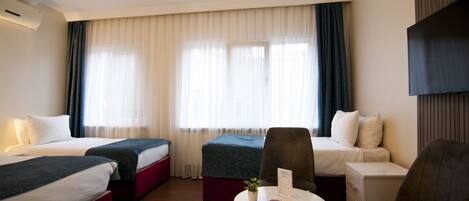 Quarto de hotel com duas camas, uma mesinha, uma cadeira e uma televisão.