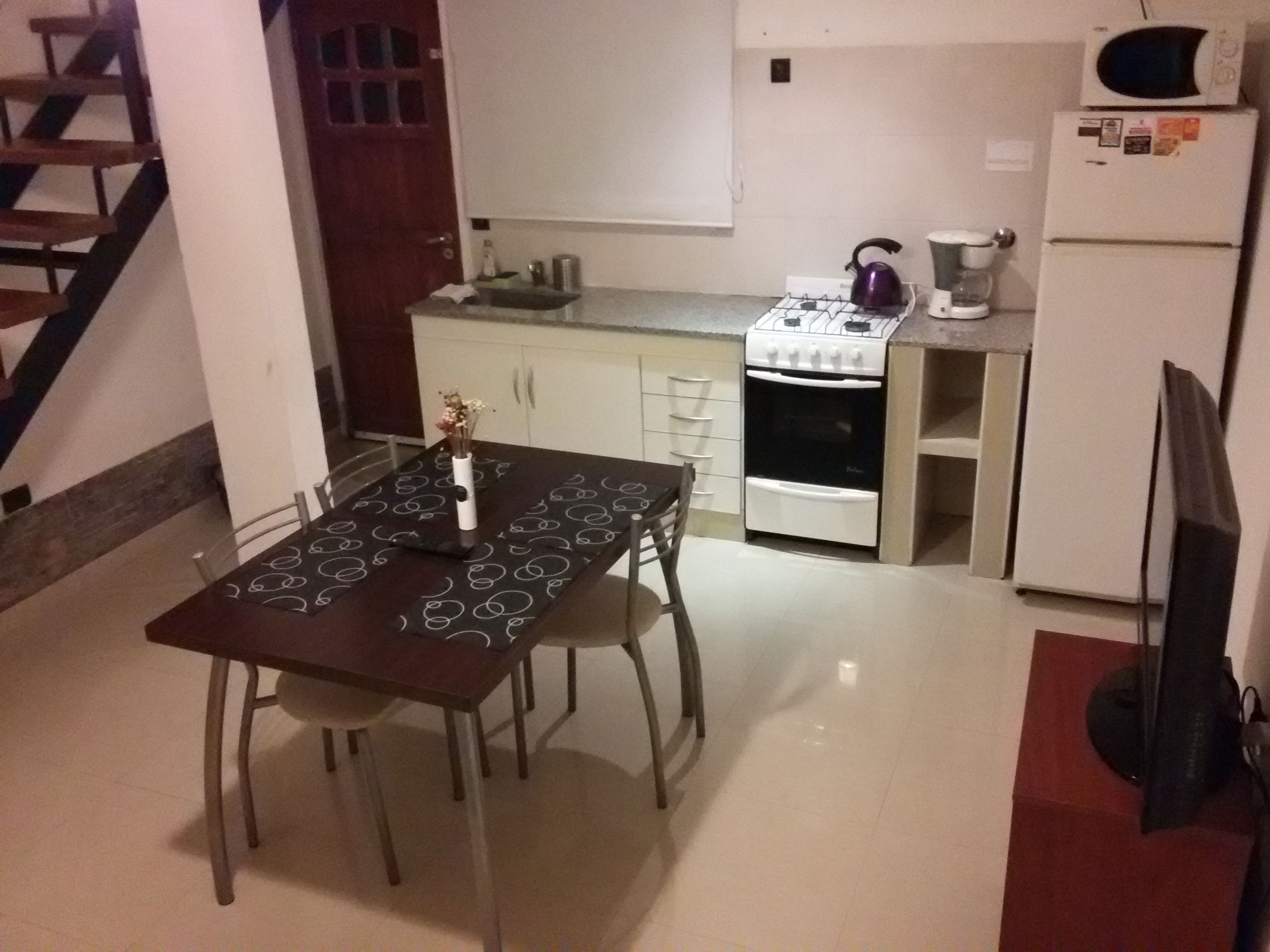Uma cozinha compacta com mesa, cadeiras, fogão, micro-ondas e geladeira.