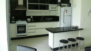 Uma cozinha moderna com armários brancos, bancada preta, forno embutido, micro-ondas, geladeira e três banquetas.