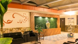 Um hall com parede de pedra, balcão de recepção, sofá de couro preto, mesa de centro e um vaso de planta.