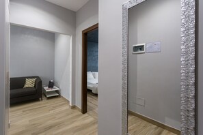 Quarto de hotel moderno com um sofá escuro, uma mesinha de cabeceira, uma cama e uma parede com textura.