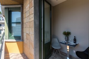 Varanda com porta de correr de vidro, uma pequena mesa com um vaso de flores e uma cadeira.