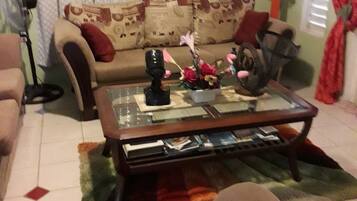 Uma sala de estar com sofá, mesa de centro, ventilador e um vaso com flores.