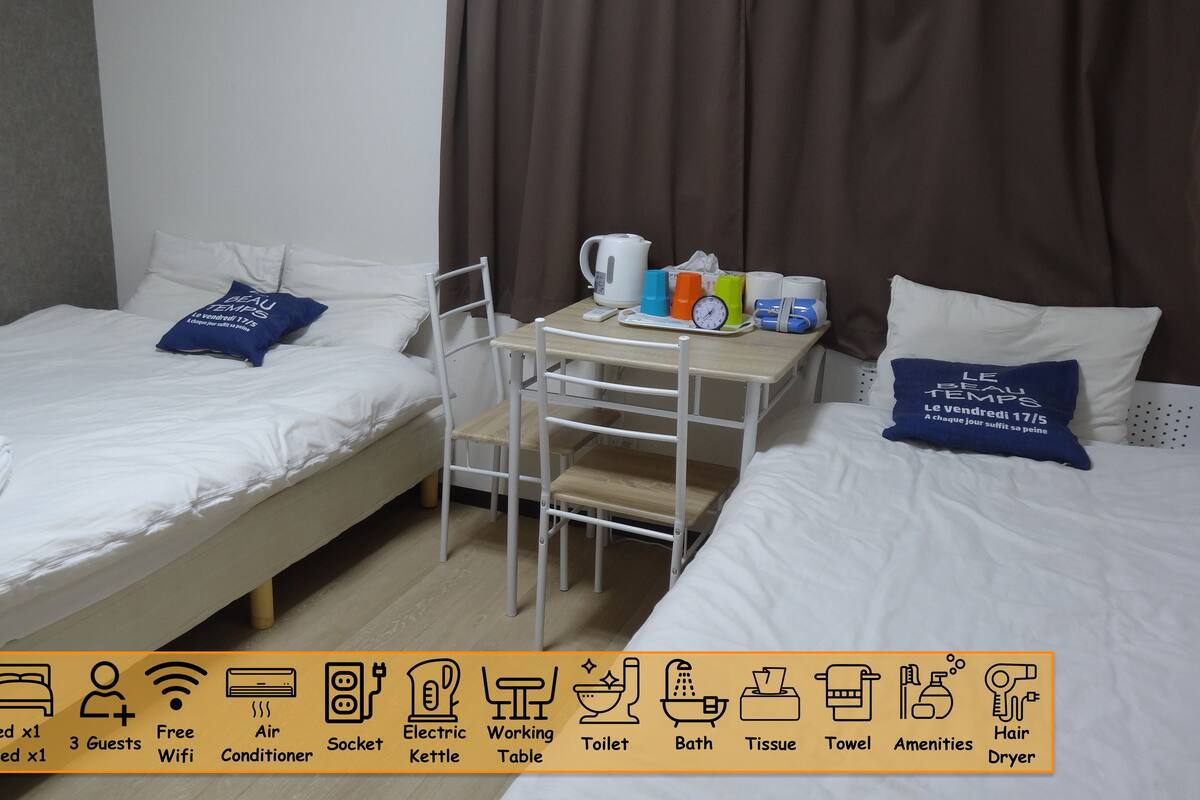 Quarto de hotel com duas camas de solteiro, uma mesinha com chaleira e chávenas, e uma cadeira. Inclui secretária, sanita, banheira, lenços de papel, toalha, artigos de higiene e secador de cabelo.