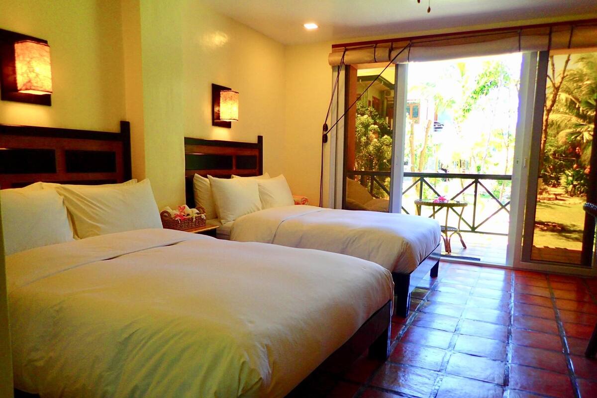 Quarto de hotel com duas camas, uma mesa de cabeceira, um abajur e vista para o exterior por uma porta de correr.