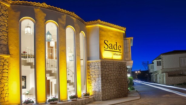 Um hotel chamado "Sade" com fachada de pedra, grandes janelas em arco e uma escadaria que leva a um andar superior.