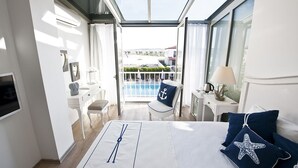 Quarto de hotel com varanda, cama com roupa de cama temática náutica, escrivaninha e uma cadeira.