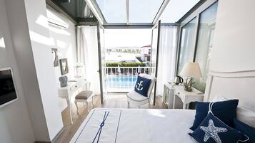 Quarto de hotel com varanda, cama com roupa de cama temática náutica, escrivaninha e uma cadeira.