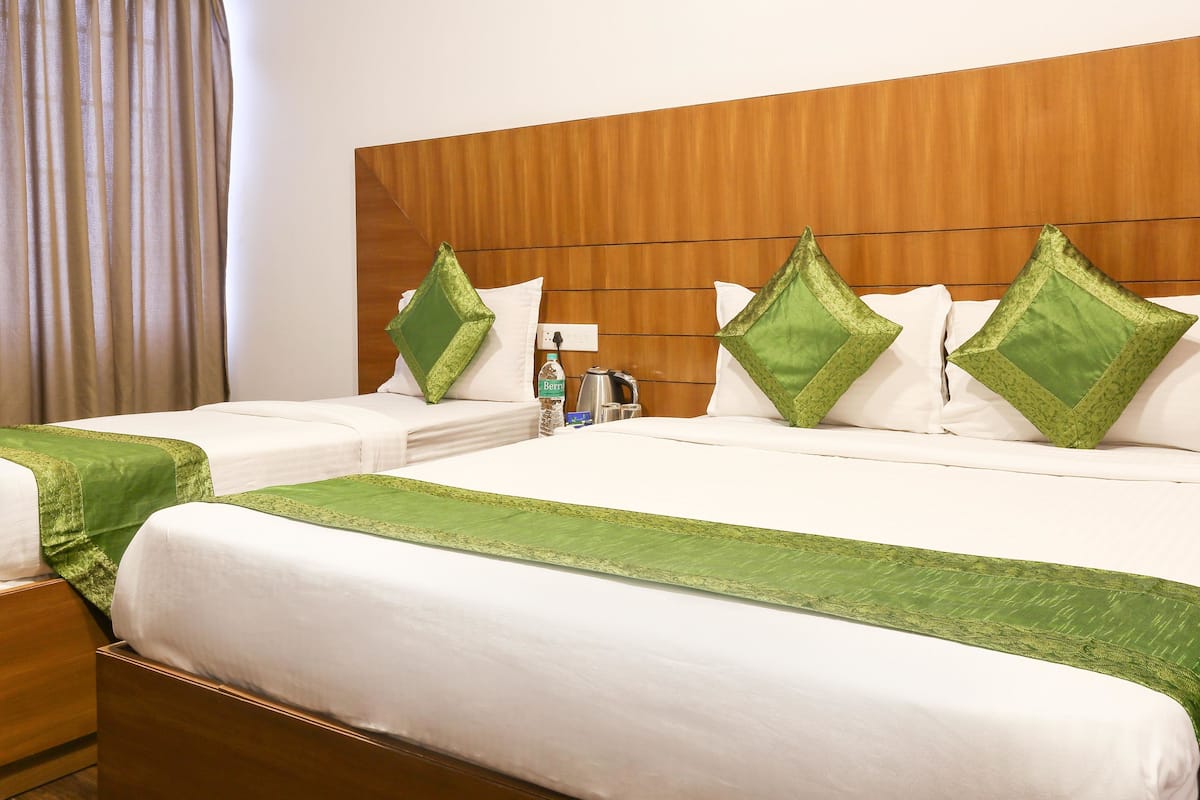 Quarto de hotel com duas camas, cabeceira de madeira e almofadas decorativas verdes.