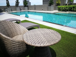 Uma área na beira da piscina com móveis de vime e uma piscina azul cristalina.