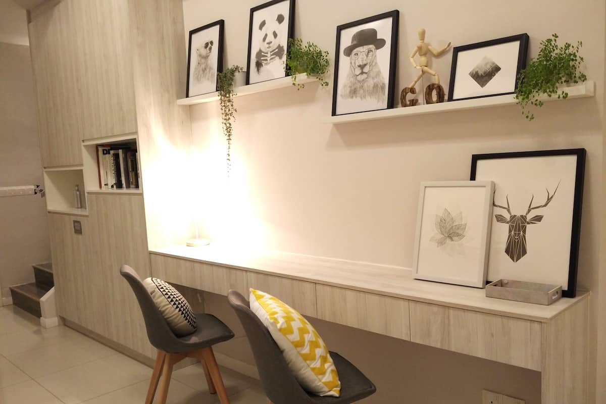 Uma sala de estar moderna com piso de madeira, duas cadeiras pretas com almofadas estampadas, um console branco com obras de arte emolduradas e uma pequena estante com livros e objetos decorativos.