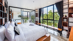 Quarto moderno com cama grande, vista para área verde e estante embutida.