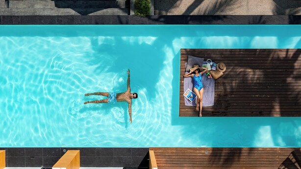 Piscina com deck de madeira e área de descanso com toalha e chapéu.