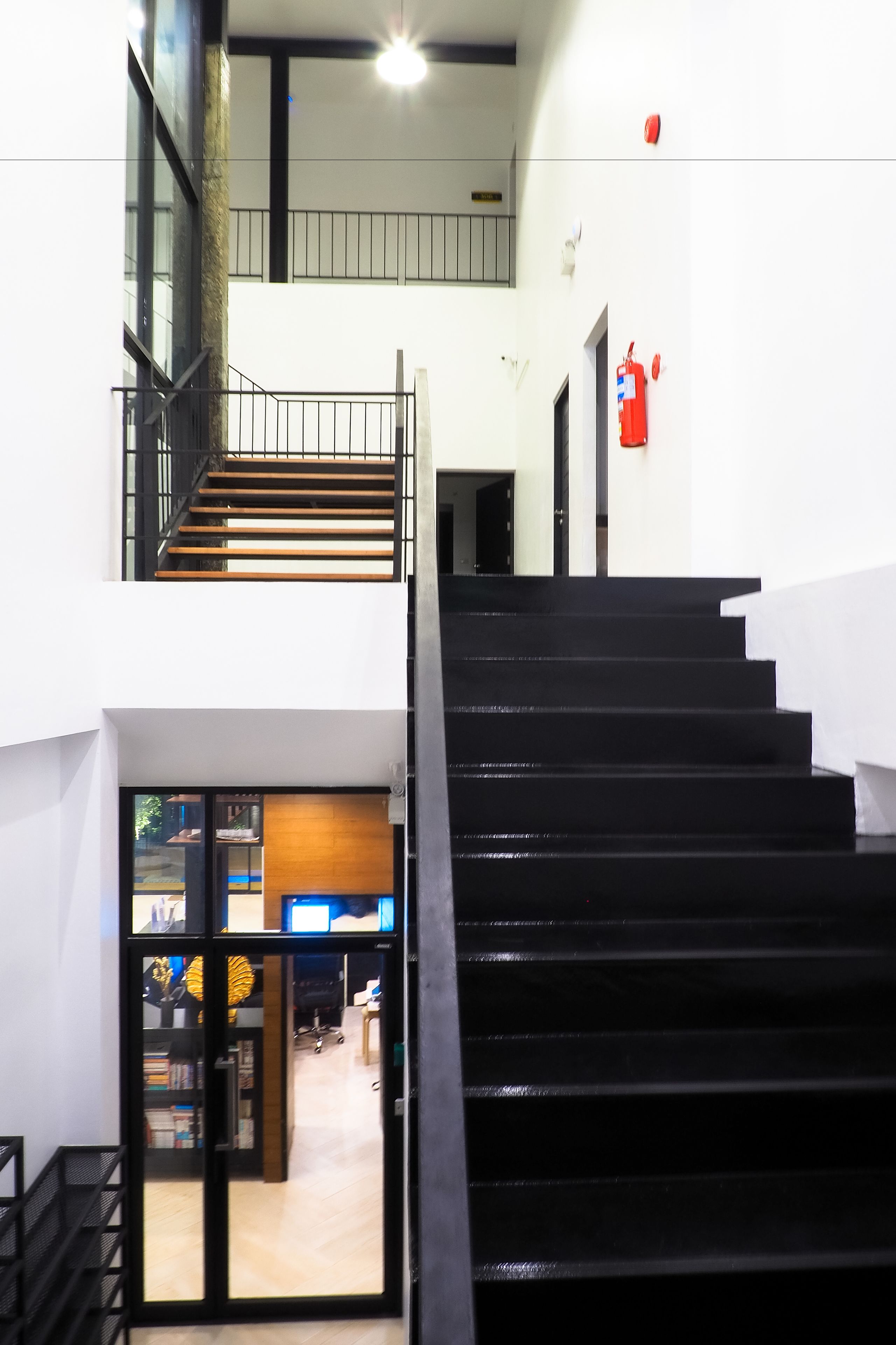 Um edifício moderno com uma escadaria que leva a um segundo andar. Há um extintor fixado na parede.