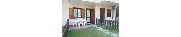 Um espaço ao ar livre pequeno com uma mesa e cadeiras, cerca de madeira e um caminho pavimentado.