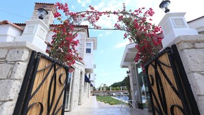 Uma entrada murada com portão de ferro forjado e arco floral.