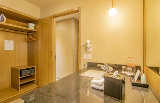 Casa de banho de hotel com bancada de granito, lavatório, espelho, porta-toalhas, secador de cabelo e um pequeno armário.