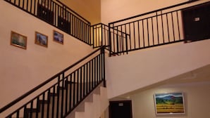 Uma escadaria com grades pretas que leva a um andar superior. Há três quadros na parede acima da escadaria.