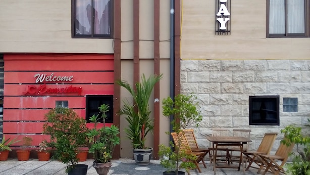 Um hotel chamado "JC Home Stay" com entrada vermelha, plantas em vasos e área de estar externa.