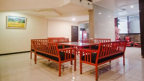 Uma área de refeições com mesa de vidro e cadeiras vermelhas, um quadro na parede e uma escada ao fundo.