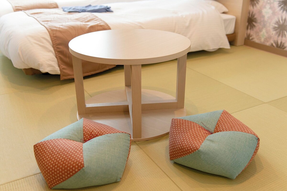 Um quarto com uma mesa redonda, duas almofadas e uma cama com cobertor.